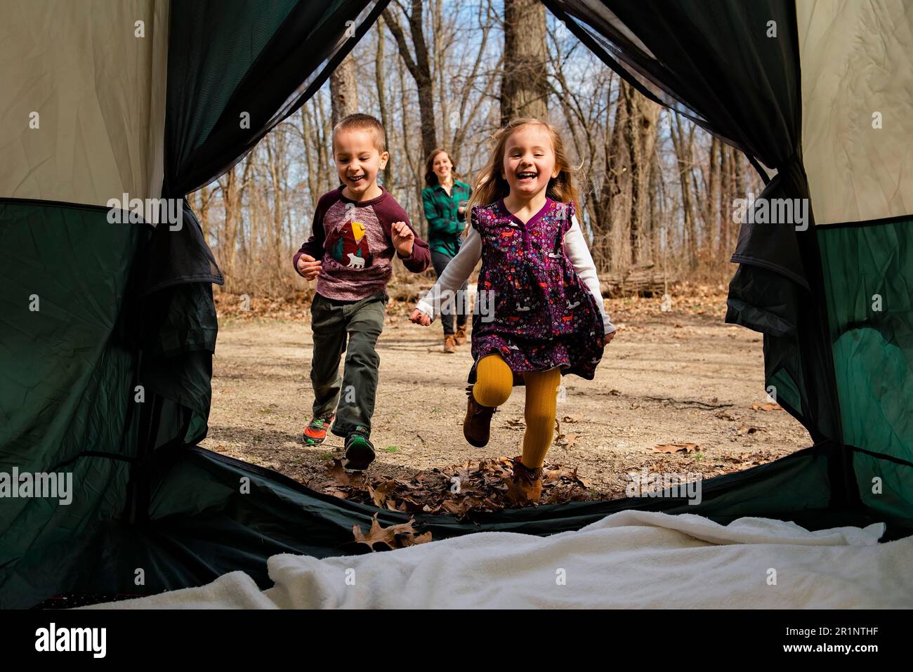 Brother and sister run laughing into tent with mother behind them Stock ...