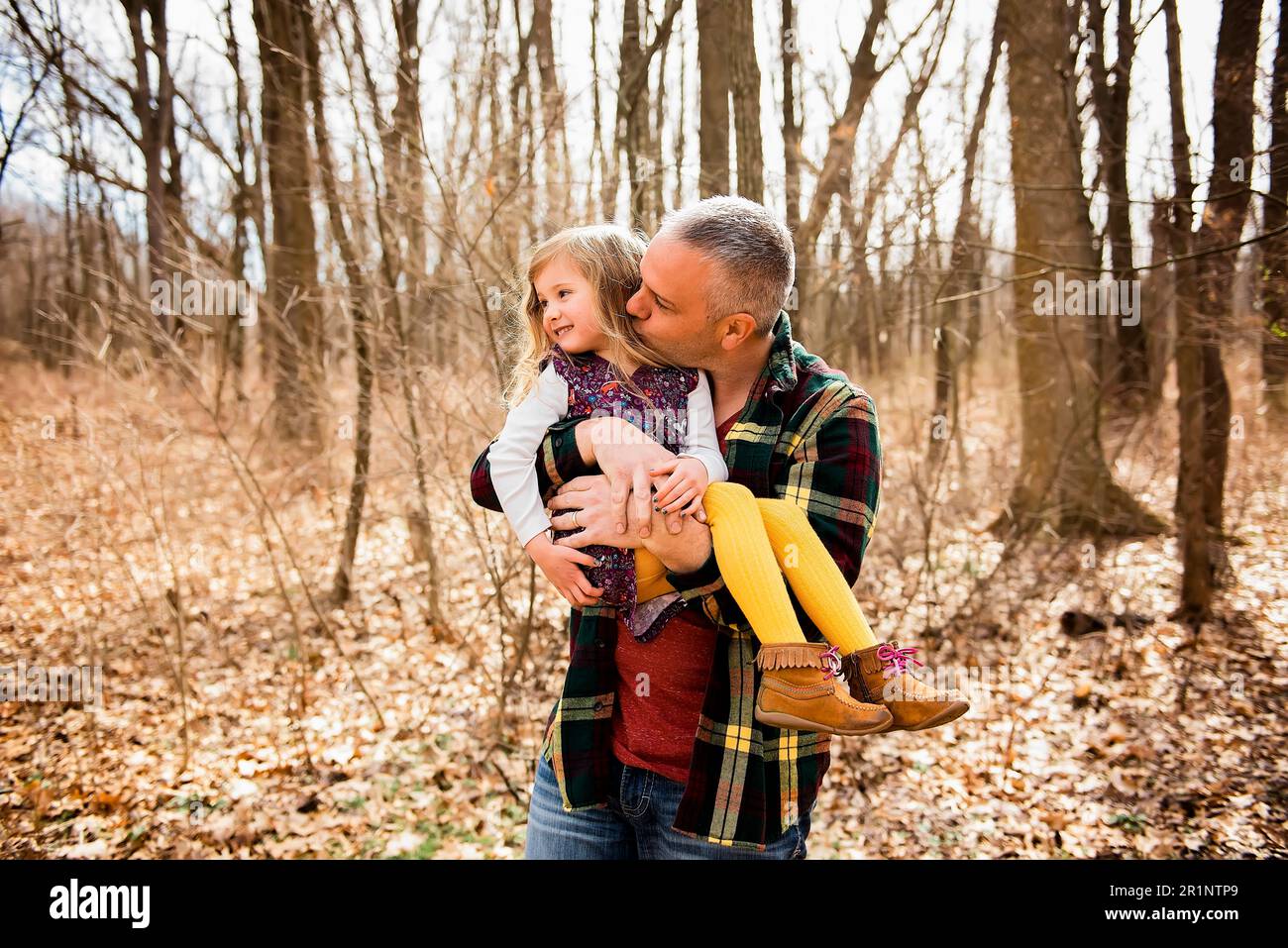 Loving father holds and kisses smiling daughter on cheek in Fall woods ...