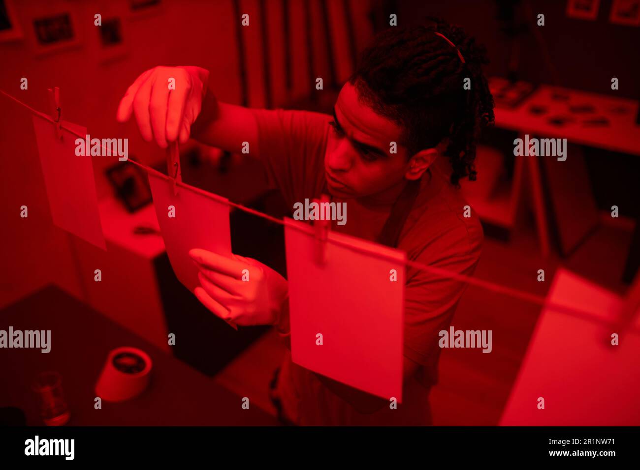 Young photographer hanging printed photos during his work in darkroom ...
