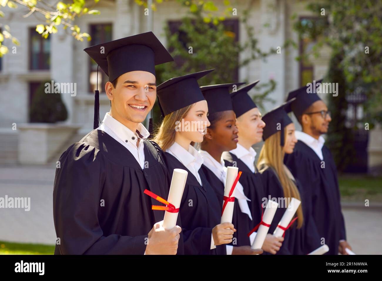 Happy graduate students dressed in black graduation gowns holding ...