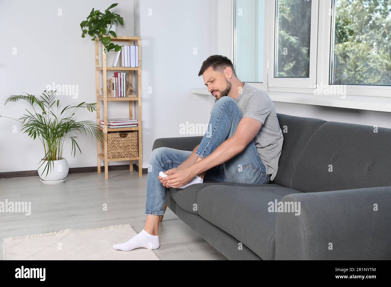 Man suffering from foot pain on sofa at home, space for text Stock ...