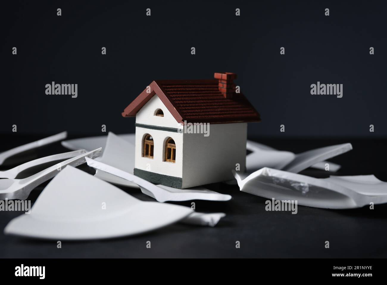 House model and broken dishes on black table depicting destruction ...