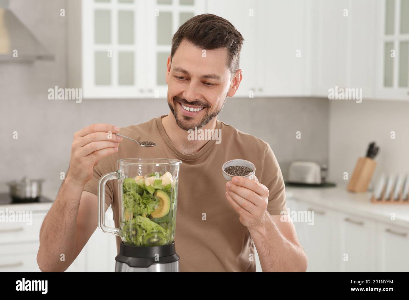 Happy man adding chia seeds into blender with ingredients for smoothie ...