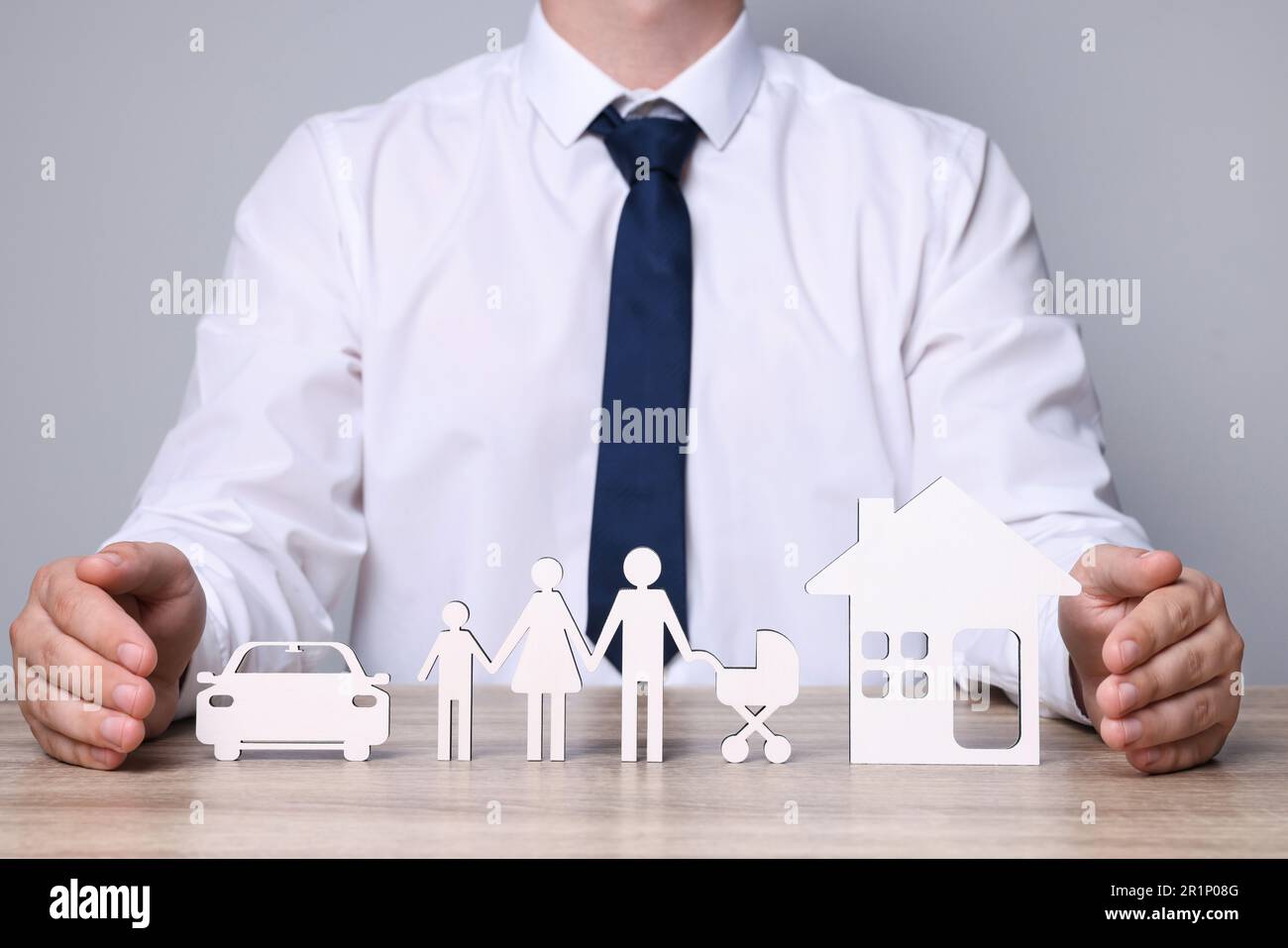 Man protecting figures of family, car and house at wooden table ...
