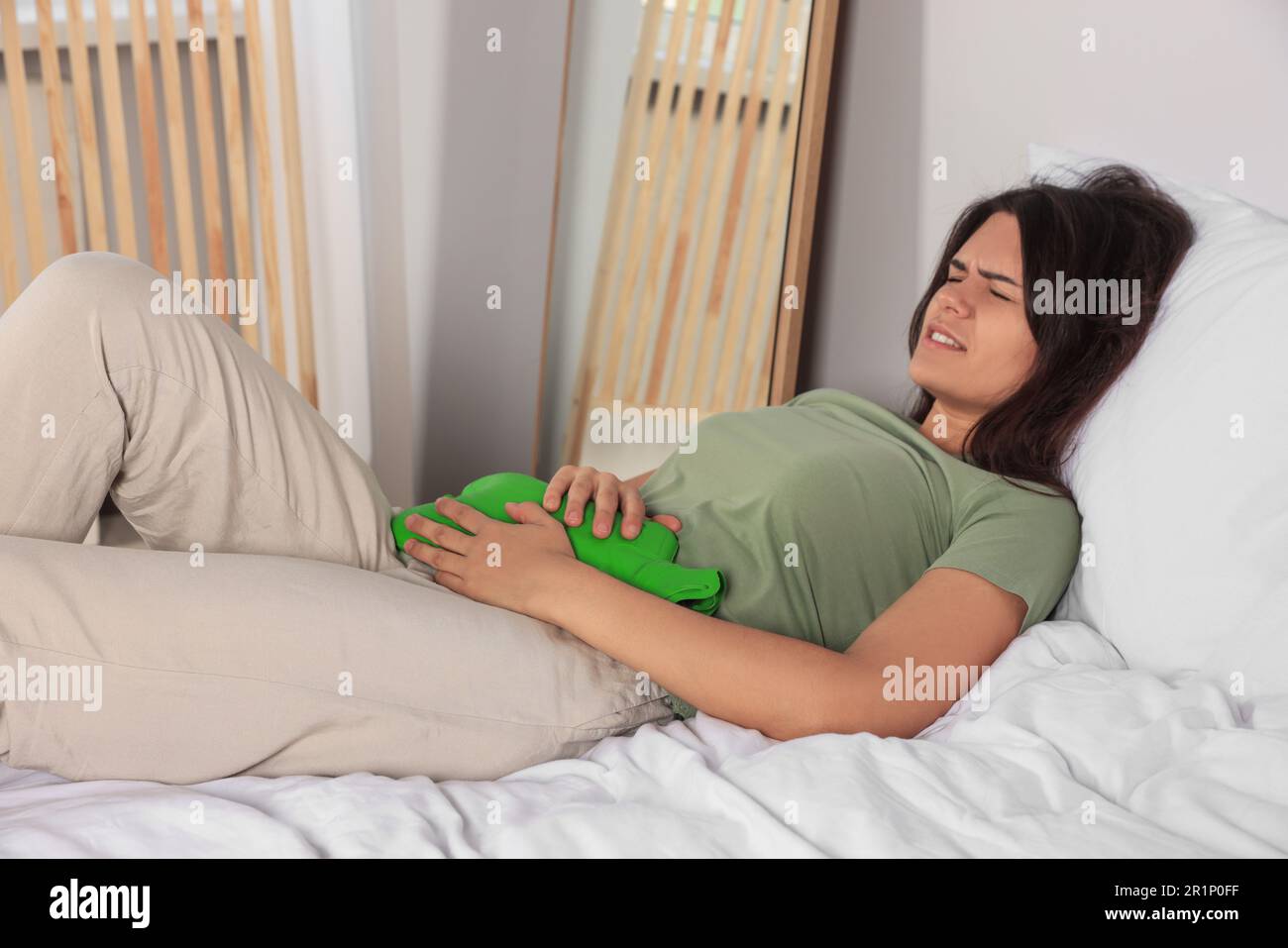 Young woman using hot water bottle to relieve cystitis pain on bed at ...