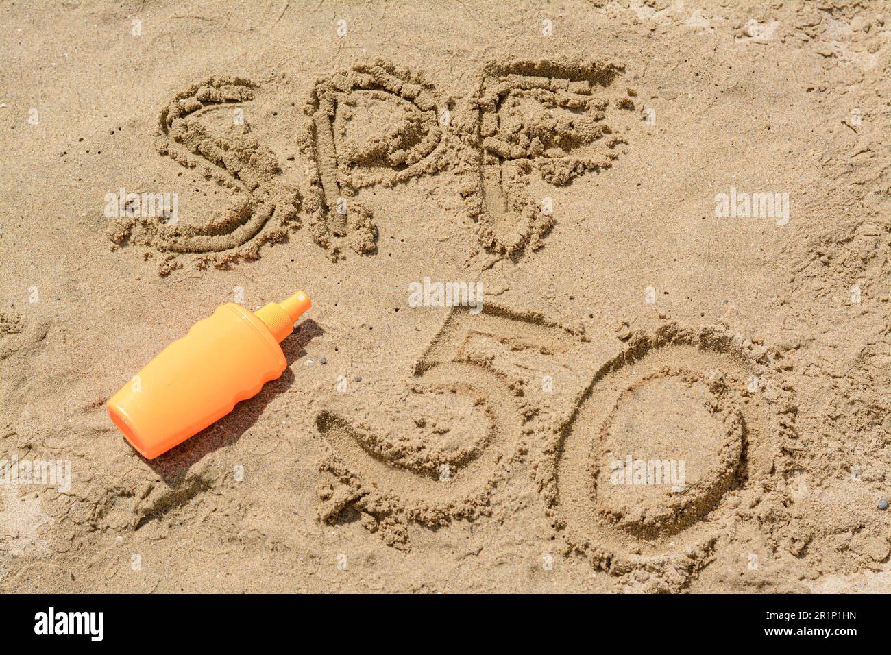 Abbreviation SPF 50 written on sand and blank bottle of sunscreen at ...