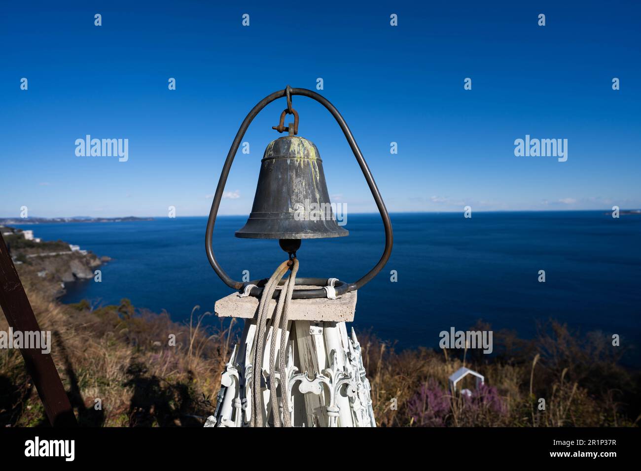A rusty metal bell suspended in midair against a backdrop of blue body ...