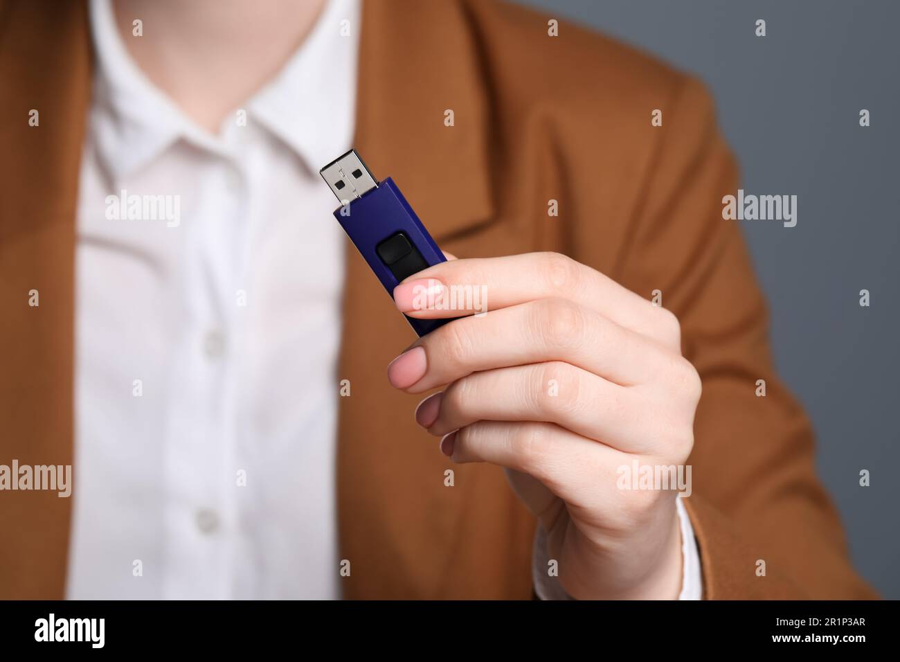 Woman holding usb flash drive against grey background, focus on hand ...