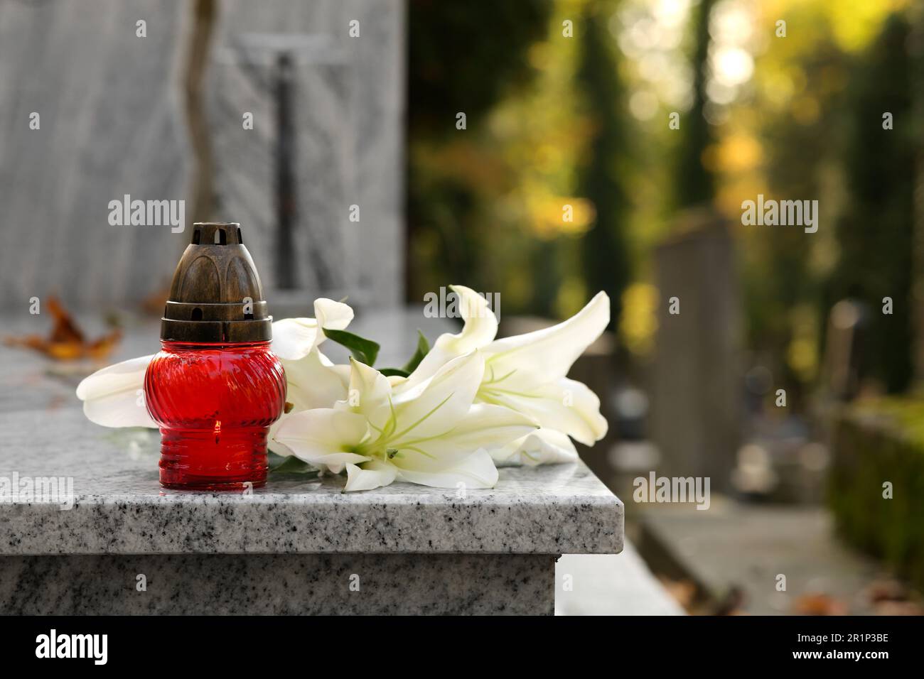 White lilies and grave lantern on granite tombstone outdoors, space for text. Funeral ceremony ...