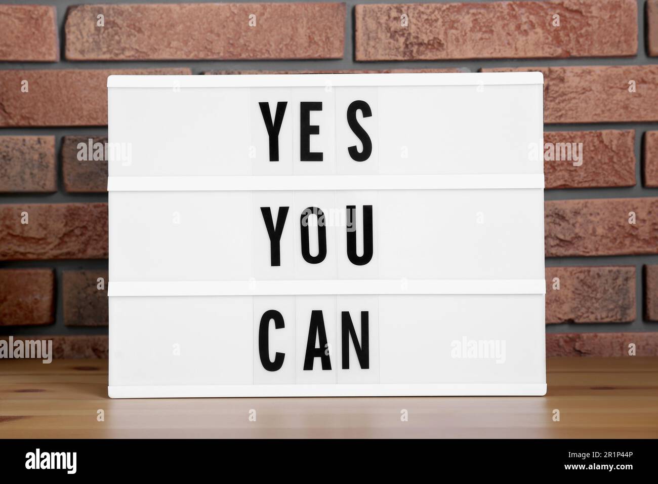 Lightbox with phrase Yes You Can on table against brick wall ...