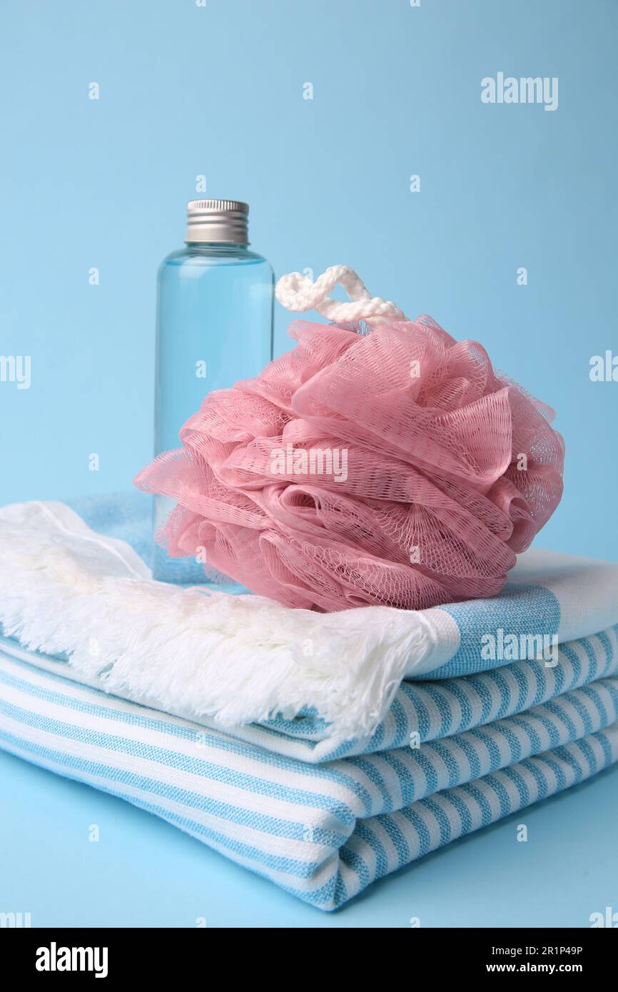 Pink shower puff, bottle of cosmetic product and towel on light blue ...