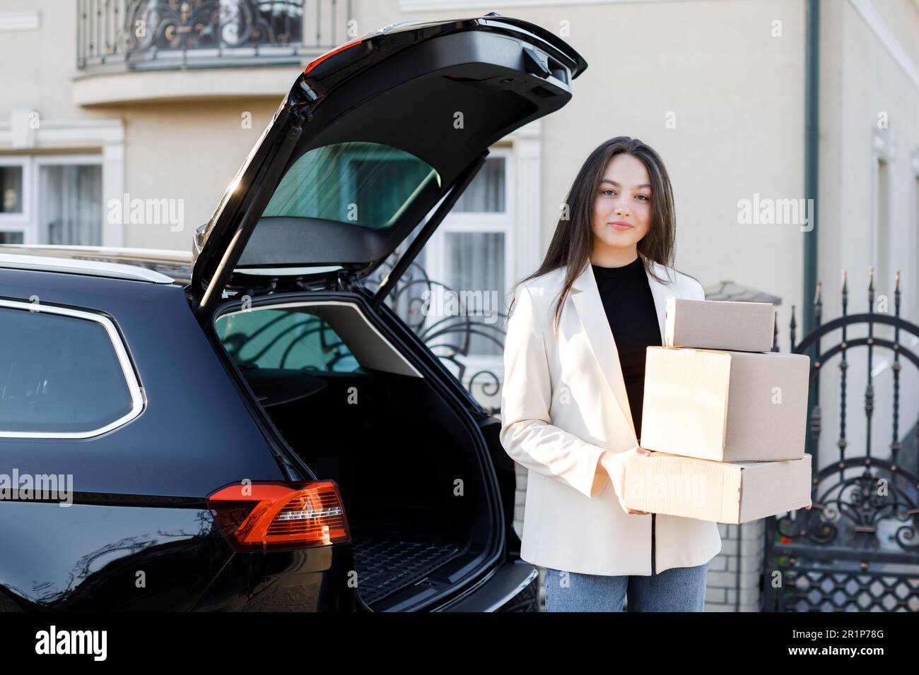 Young business woman picking up parcels from a car trunk, coming home ...