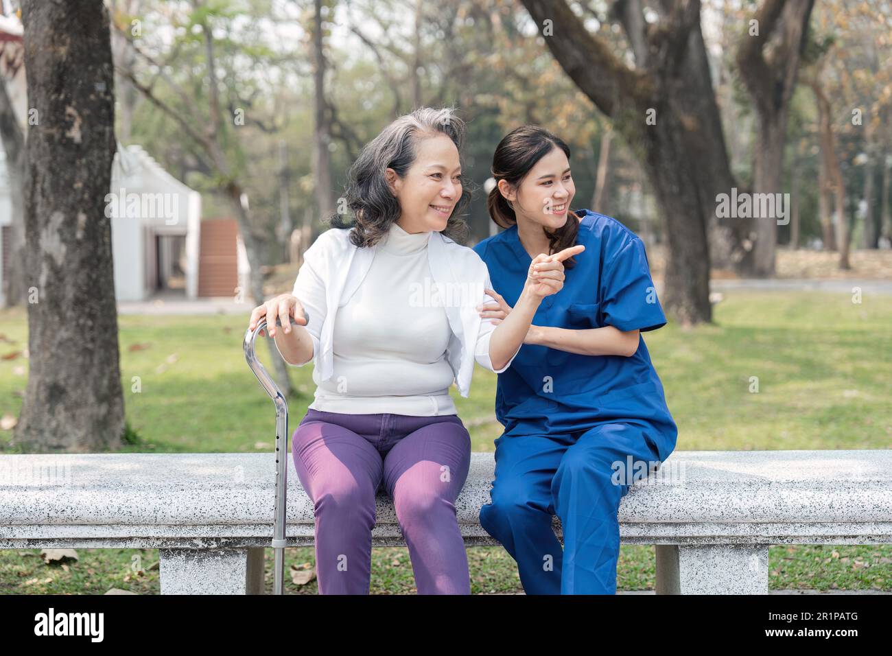 Asian female caregiver is talking while sitting on a bench in a ...