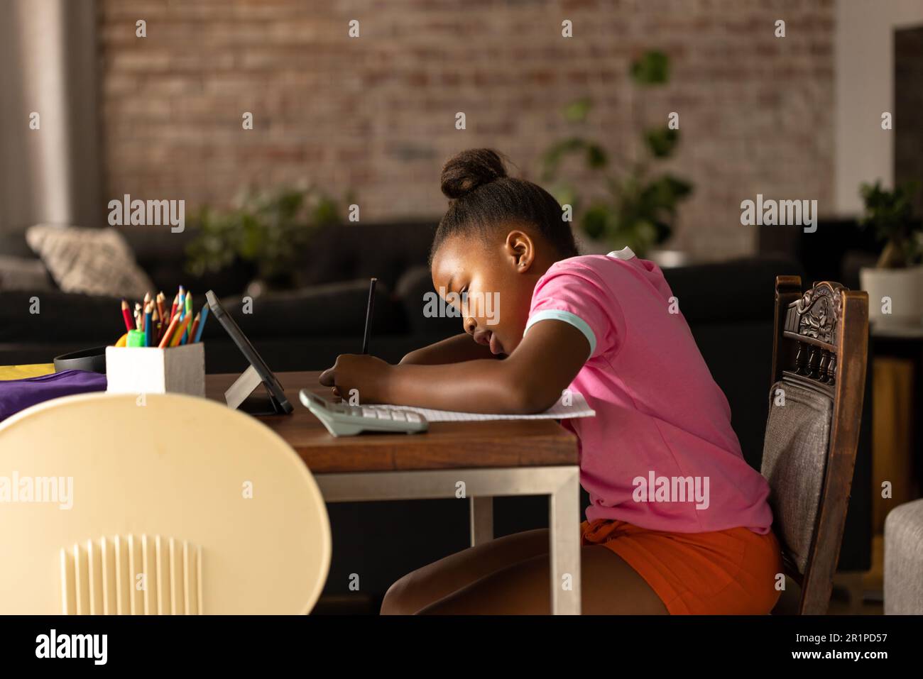 Happy african american girl sitting at dining table doing schoolwork ...