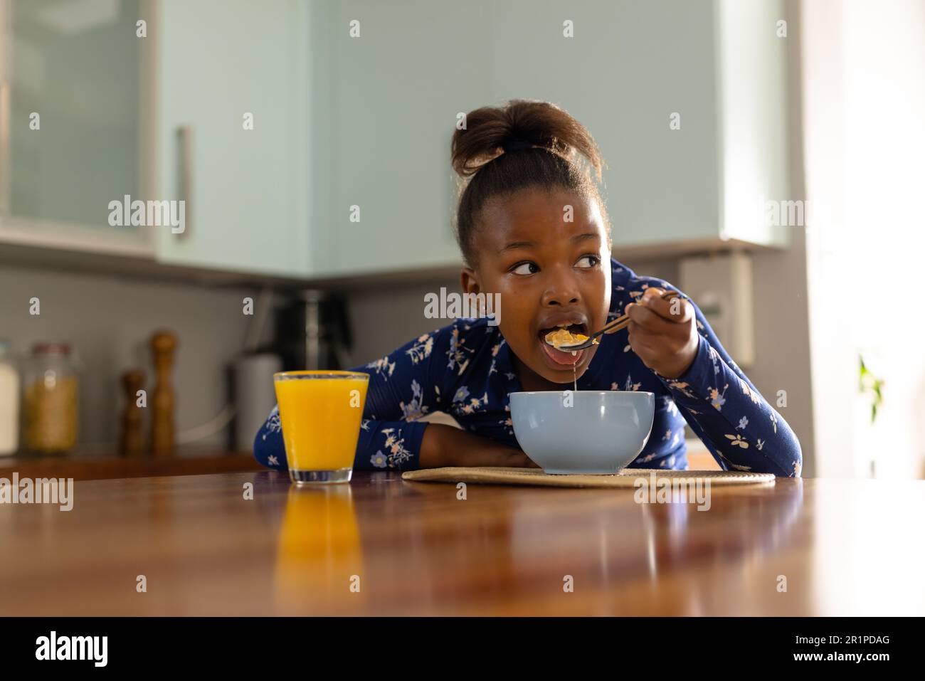 Happy african american girl eating breakfast cereal sitting in kitchen and looking away Stock ...
