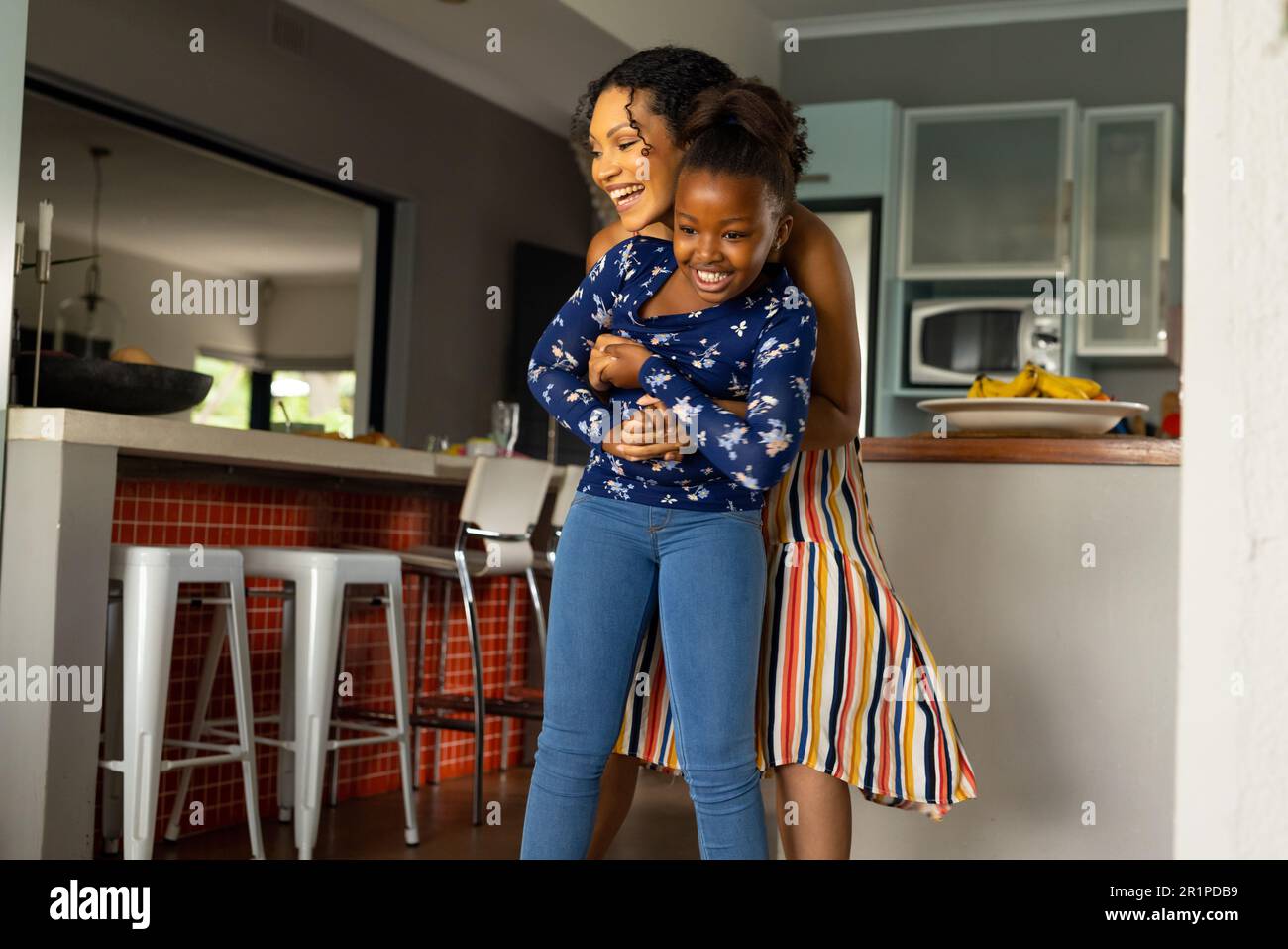 Happy african american mother and daughter having fun dancing together and hugging in kitchen ...