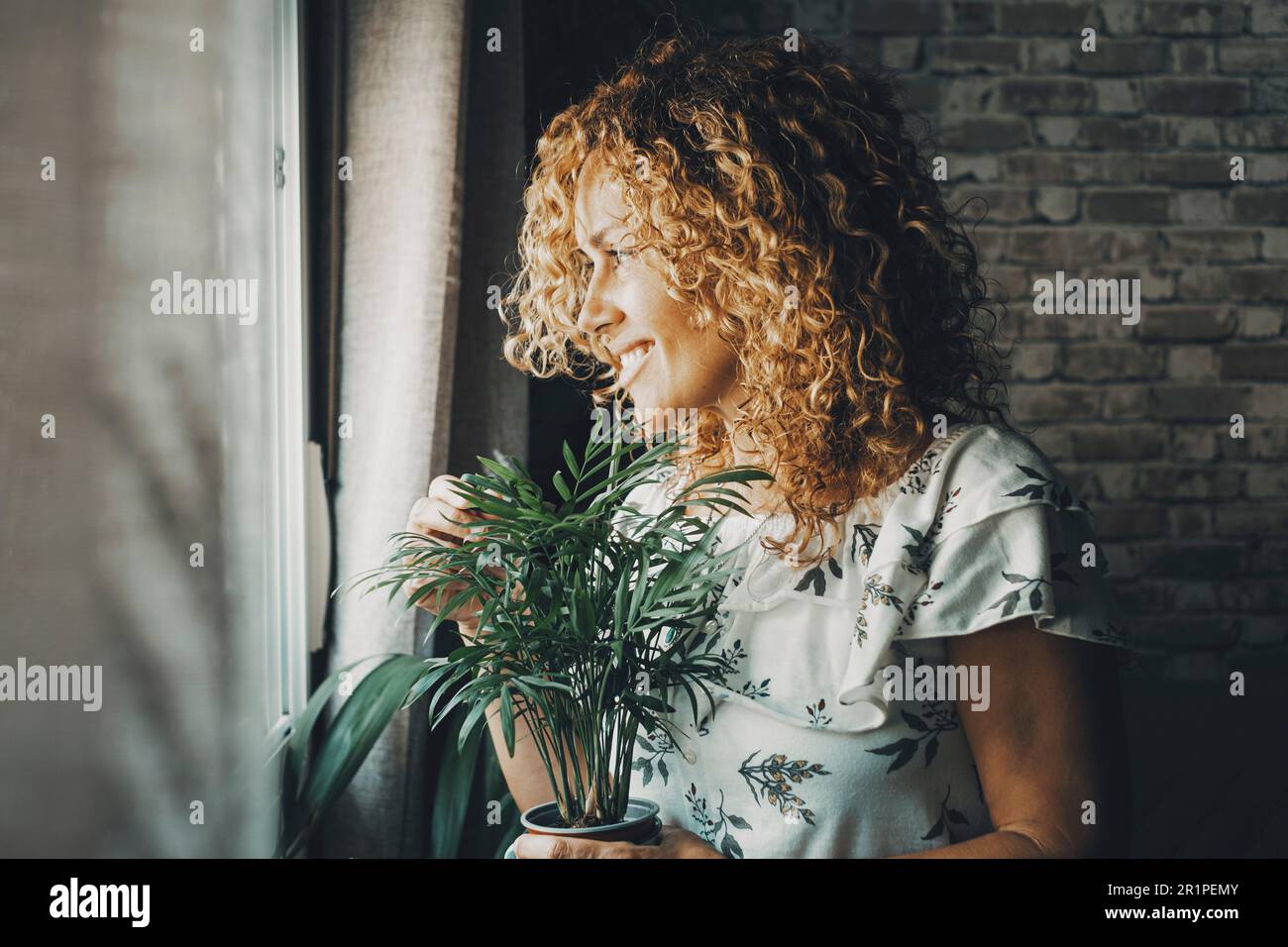 Happy woman at home looking outside the window and smiling inside dark ...