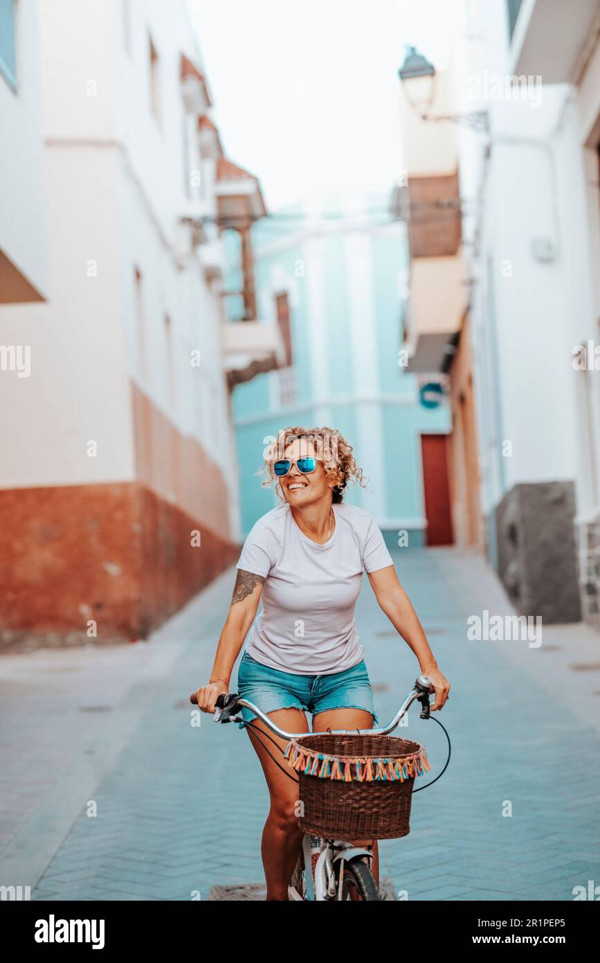 Happy cheerful young woman riding bike in the street in town with smile ...
