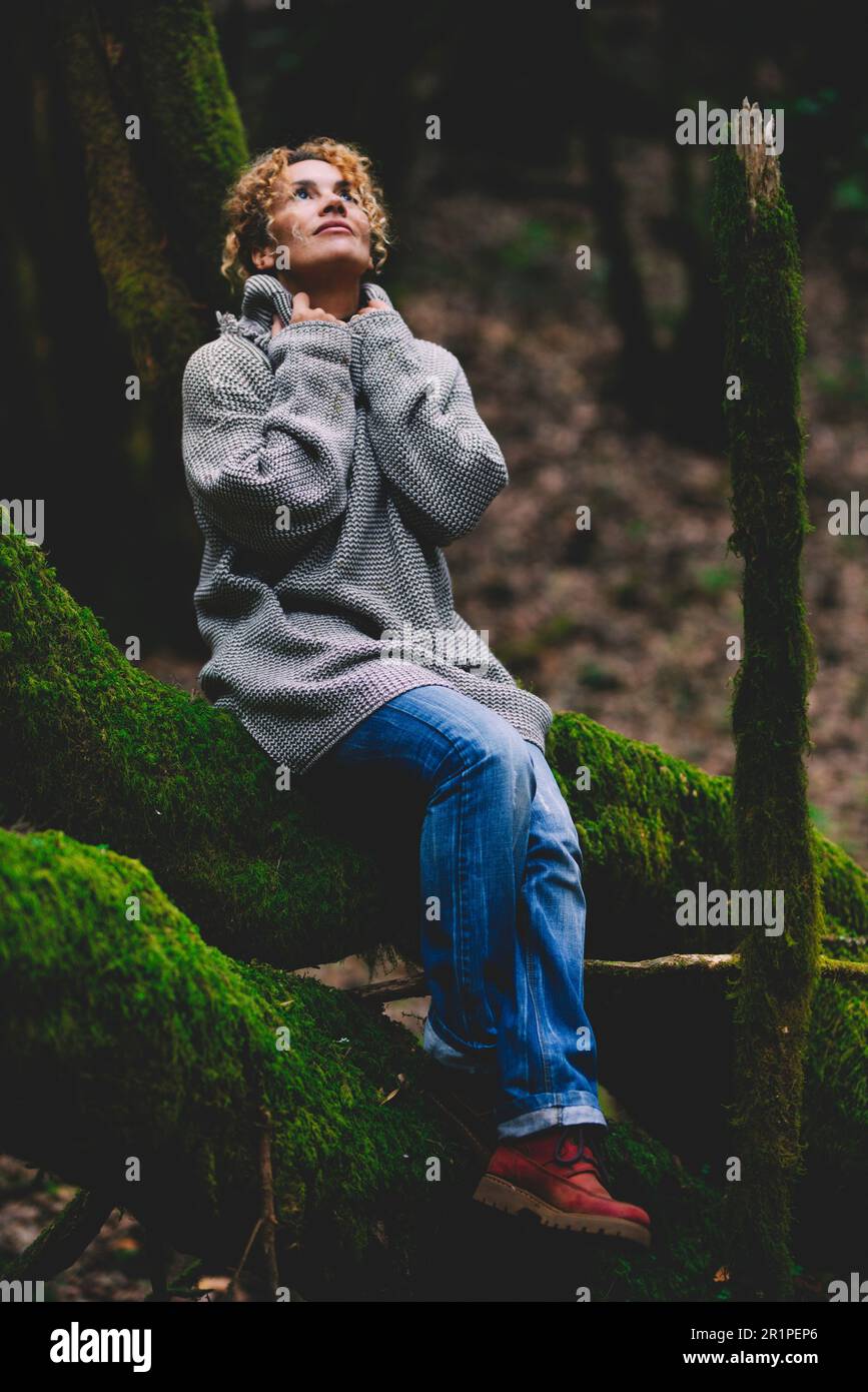One serene happy woman sitting on a green wild tree trunk looking up ...