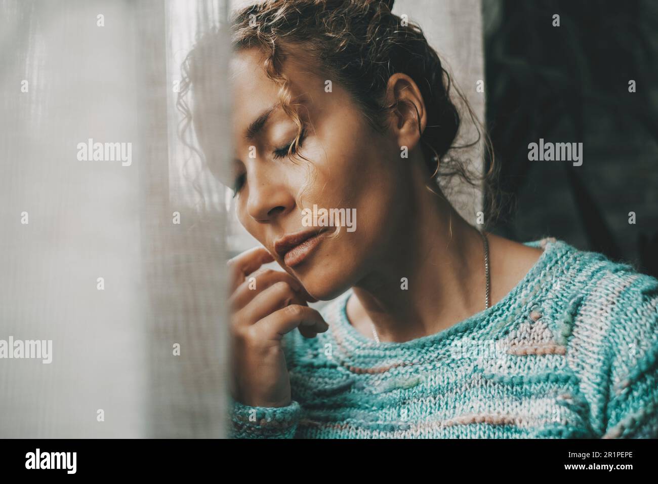 Exhausted and sad woman alone at home near the window with closed eyes ...