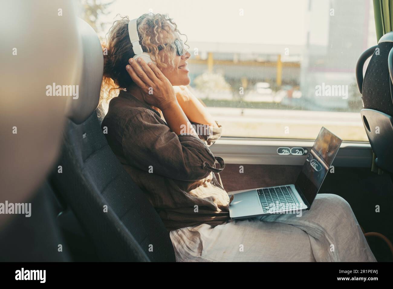 One woman listening music with headphones and computer sitting inside public bus transport ...