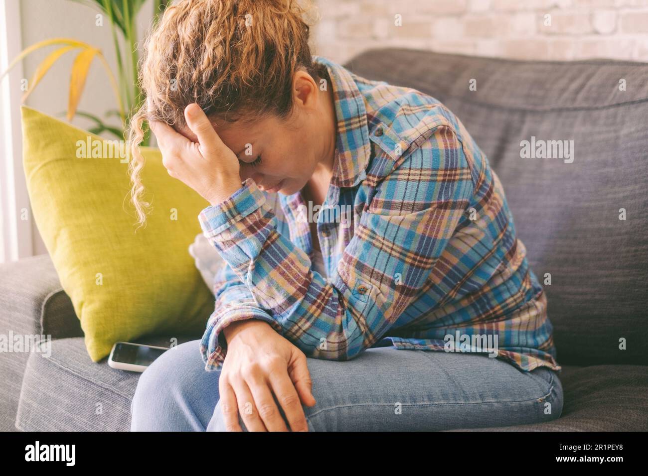 One exhausted and stressed woman at home sitting on the sofa touching ...