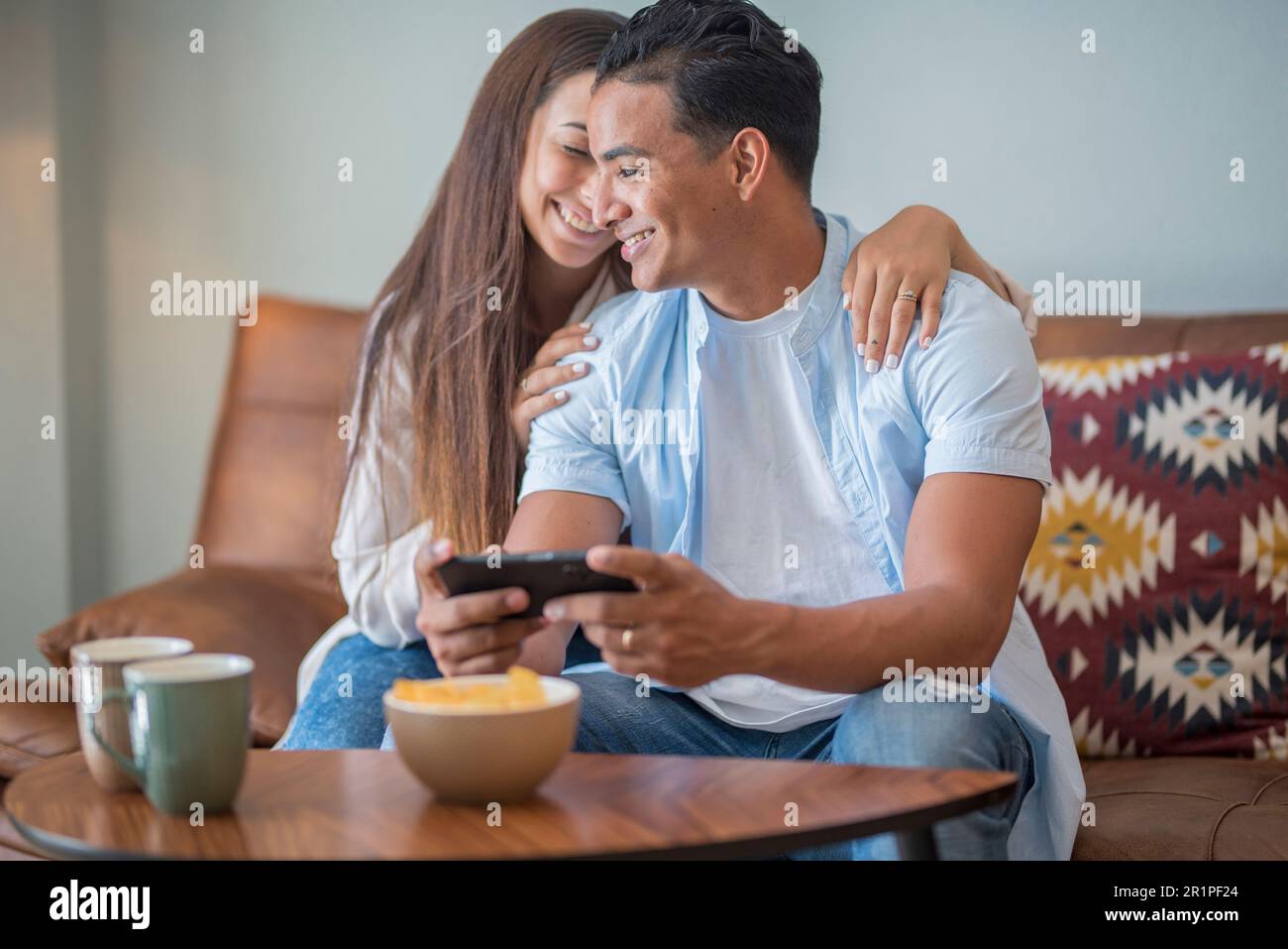 Young couple watching online content in a smart phone sitting on a sofa ...