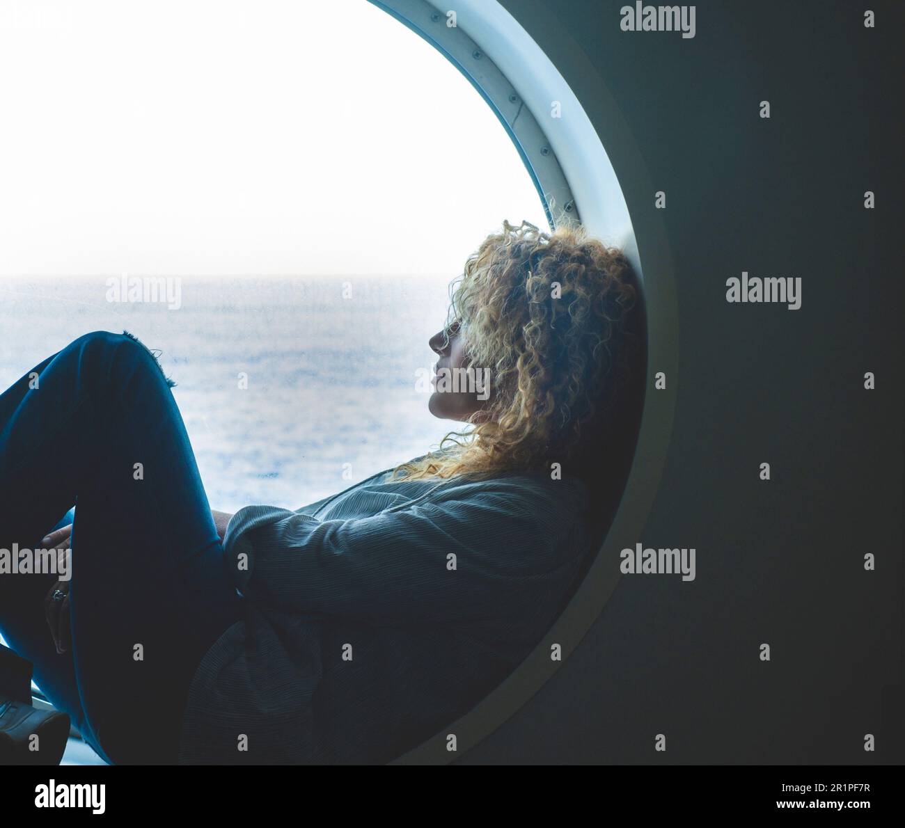 Serene woman sitting inside a porthole in the boat cruise ferry ...