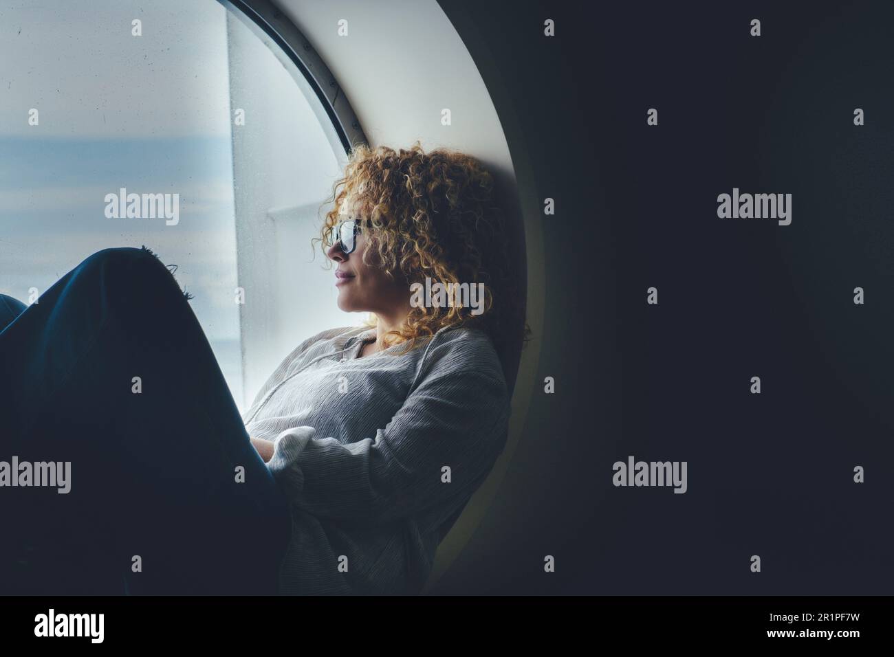 Happy woman enjoying relax and travel sitting on a porthole and looking ...
