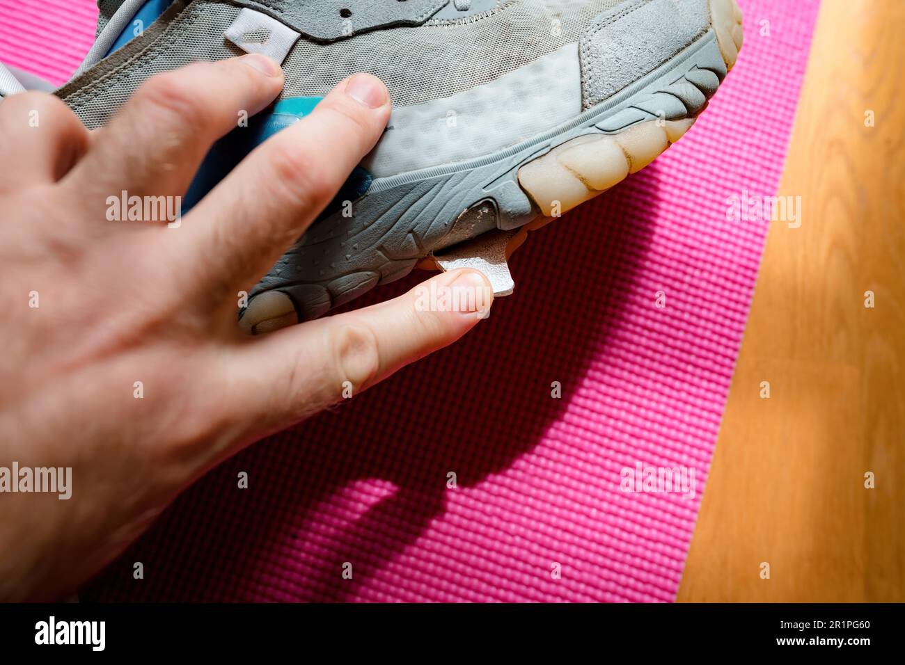 A man carefully inspects a ripped running shoe, his finger touching the ...