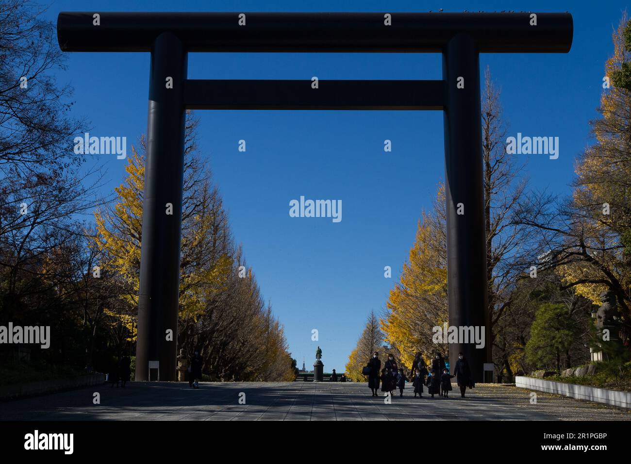 Mothers and kindergarten children walk under the large iron torii gate ...