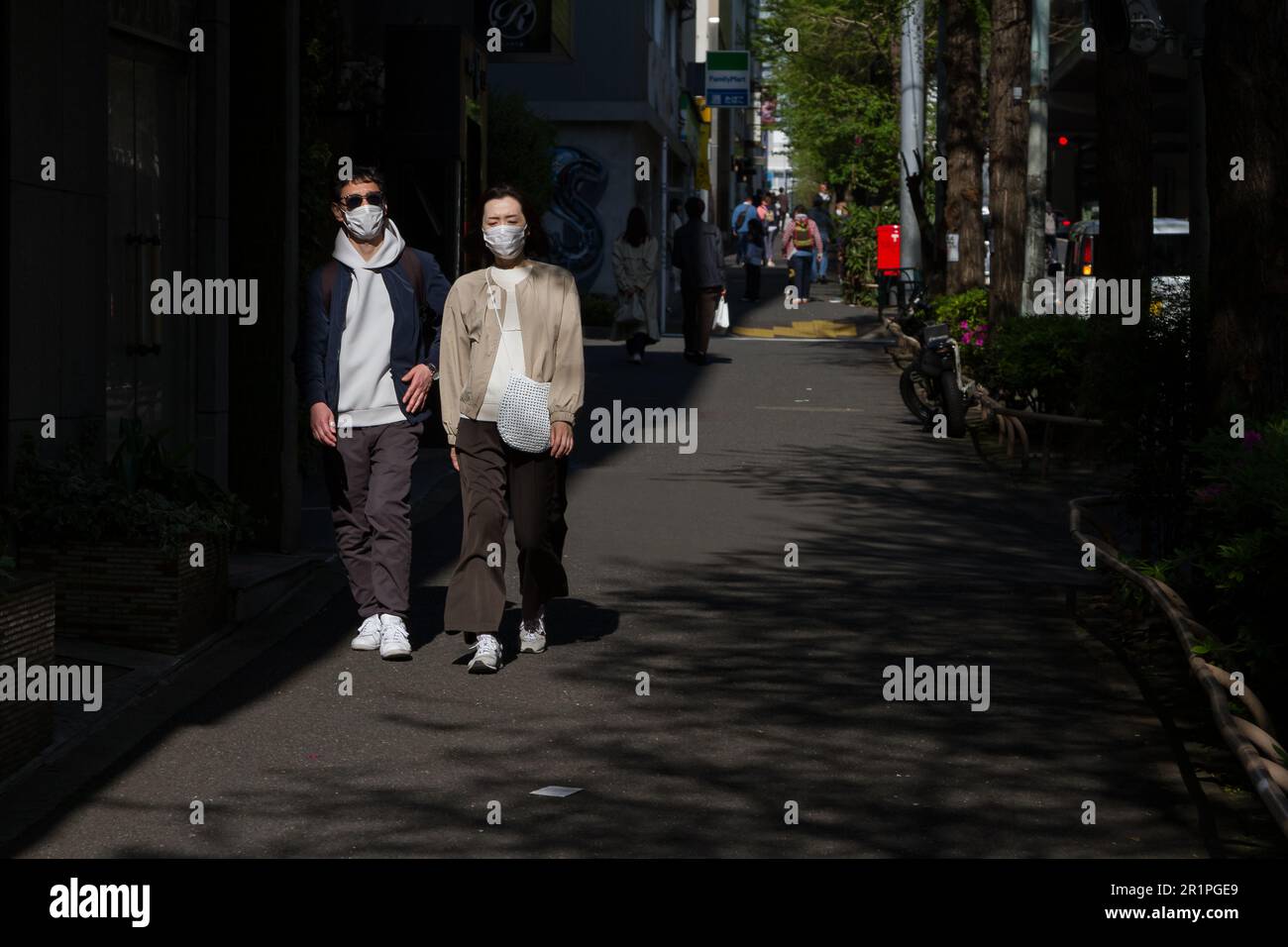 A Japanese couple walk in the street wearing surgical masks. Roppongi ...