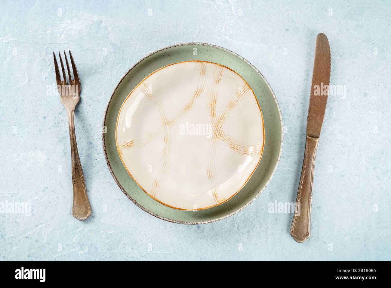 An empty plate with a gold rim, with silverware, overhead flat lay shot ...