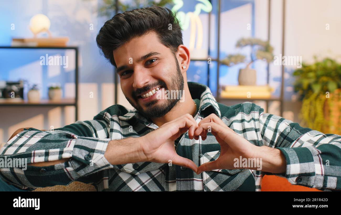 I love you. Happy indian man at home living room couch makes symbol of ...