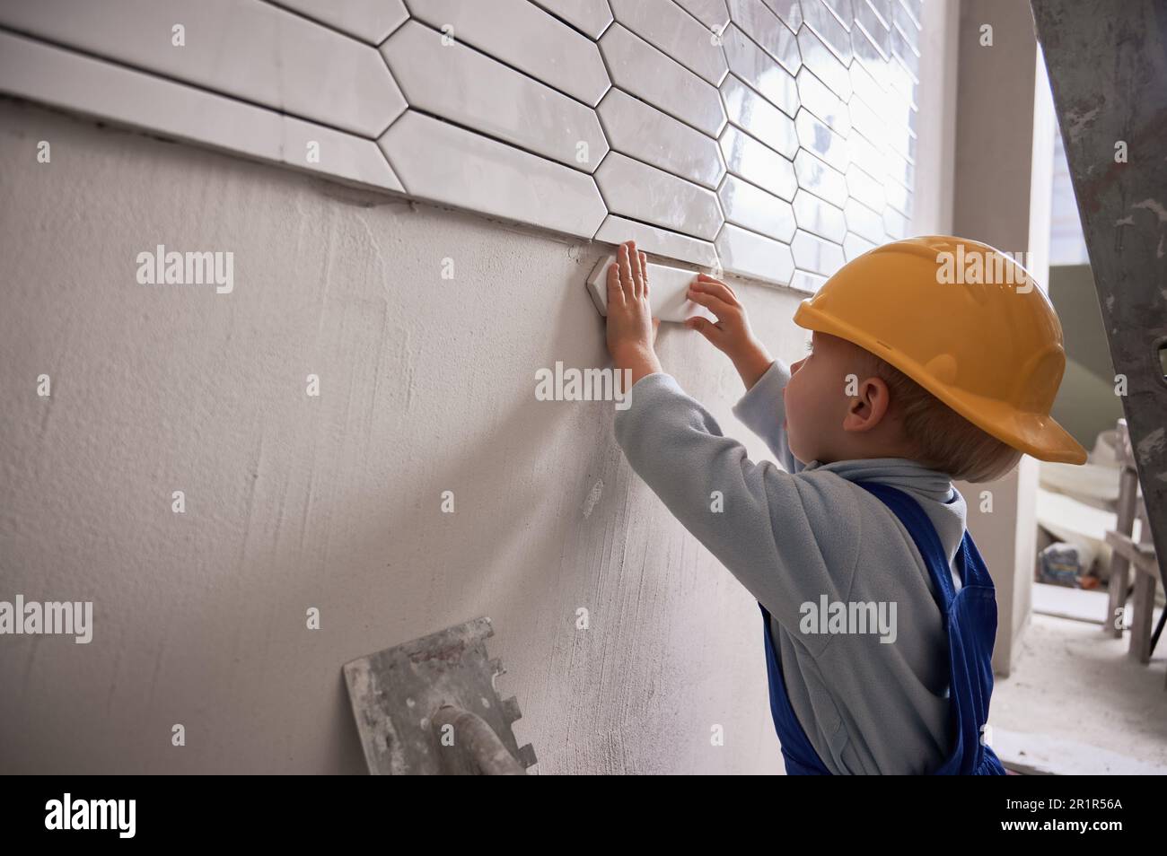 Little boy construction worker installing ceramic tile on the wall in ...