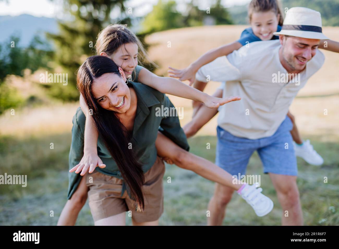 Happy parents giving their children piggyback ride in summer in nature ...