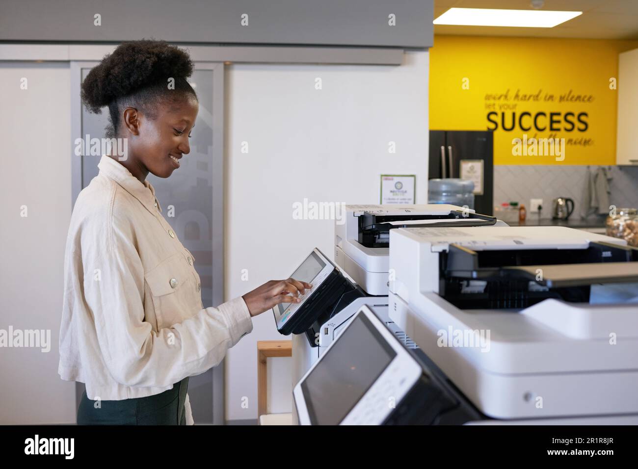Young Black woman uses photocopier machine in shared office workspace ...