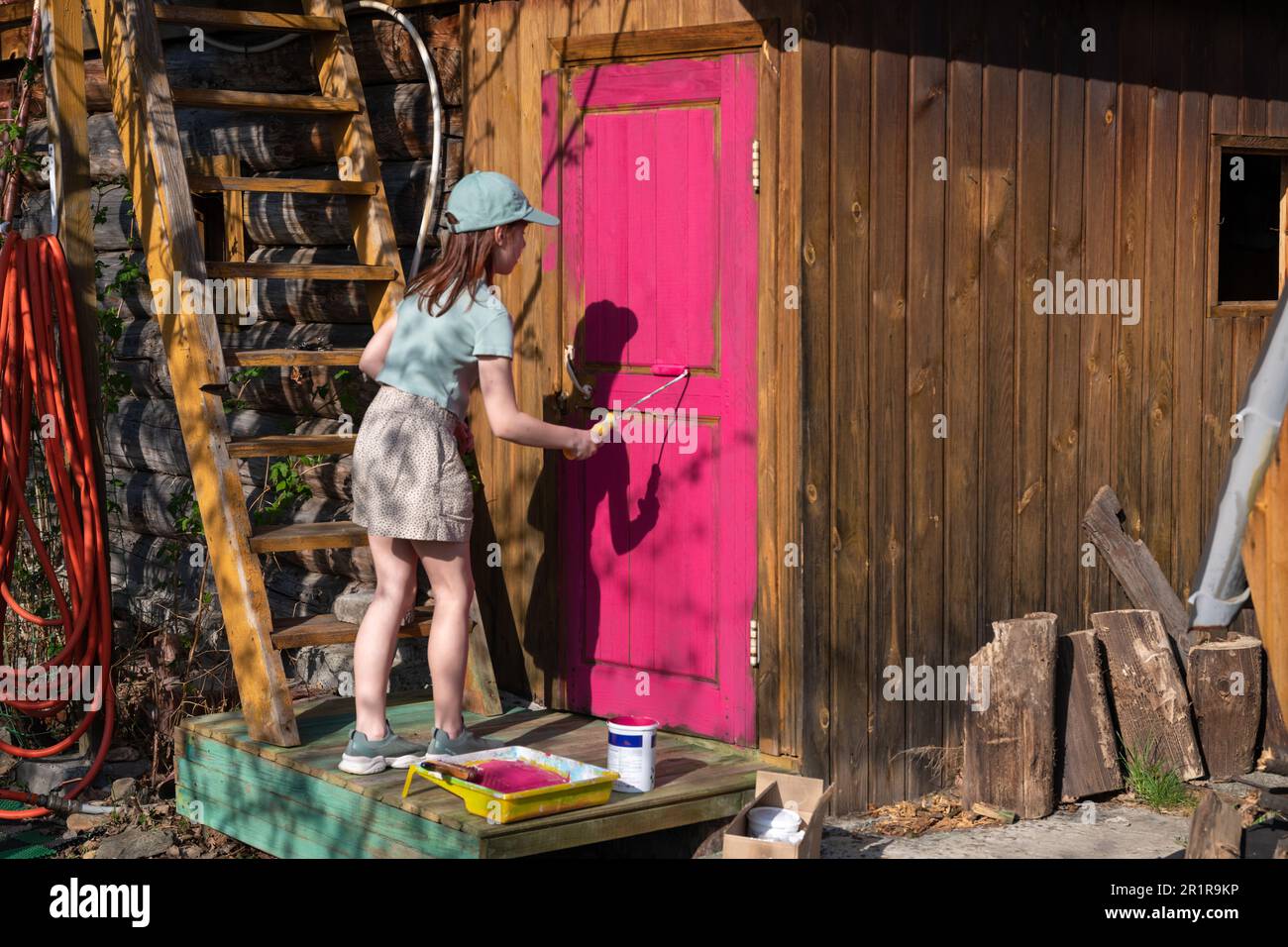 Cute girl painting the door of a wooden house in a bright purple, pink ...