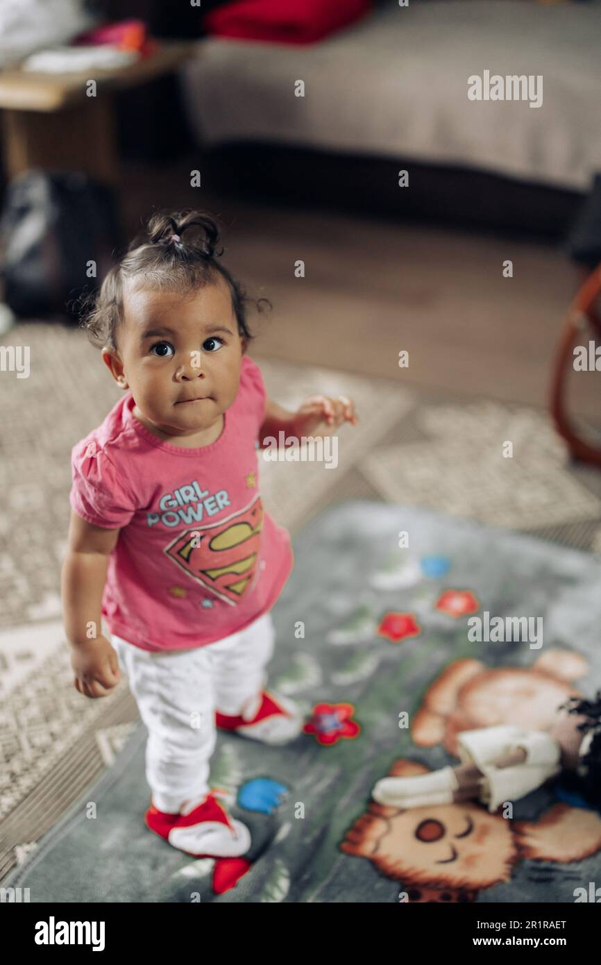 Baby girl from interracial marriage plays with toys in room. Top view ...