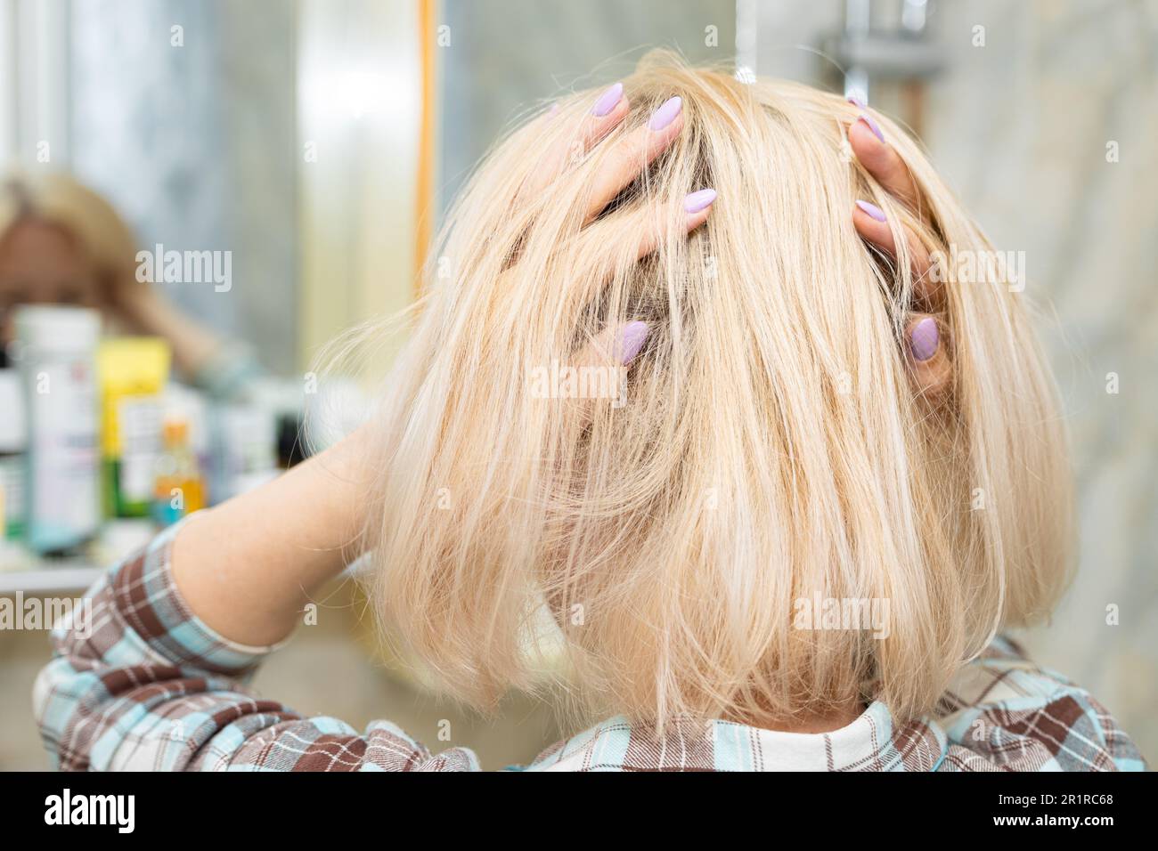 woman fixing her hair standing in front of a mirror. girl fixing her ...