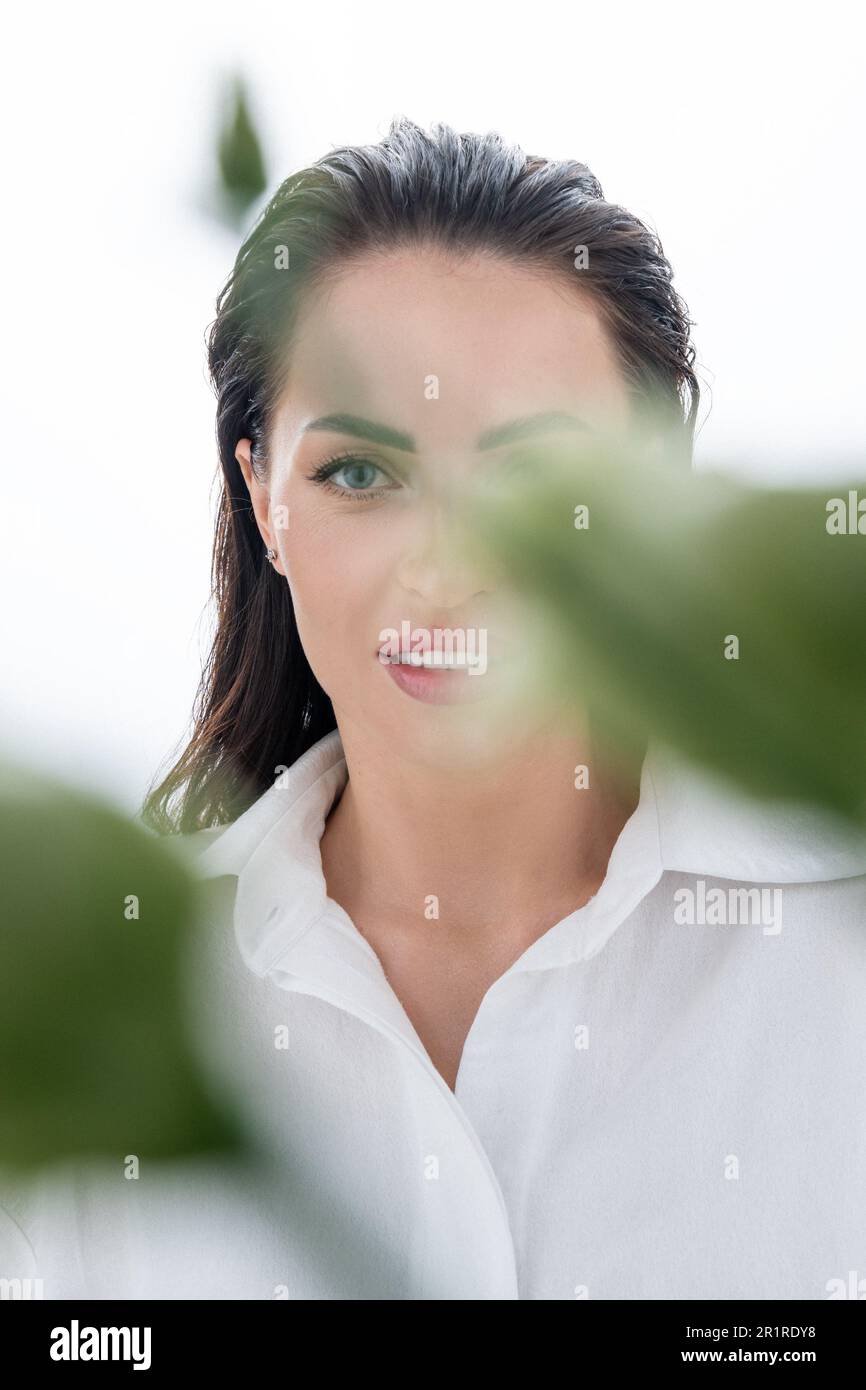 Portrait of a beautiful woman with her face partly obscured by a plant ...
