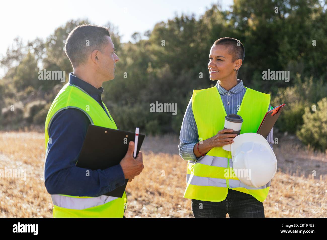 Two engineers talking while working together outdoors in the field ...