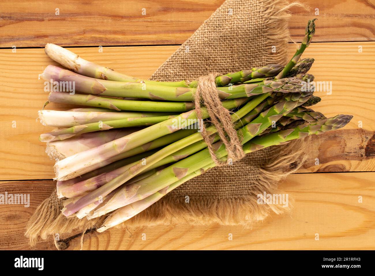 Several stalks of organic asparagus with jute napkin on wooden table ...
