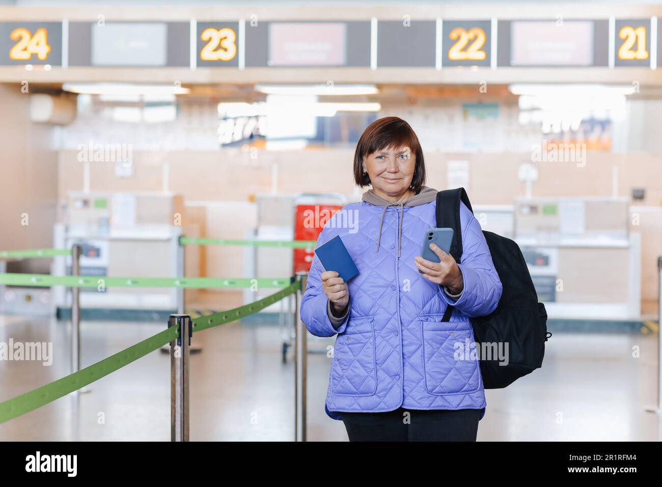 Middle aged woman traveler with backpack holds passport, uses cellphone ...