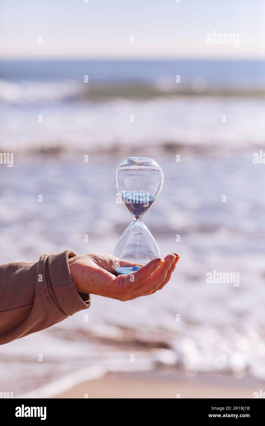 Time is running fast. Hourglass with blue sand inside in mature woman's ...