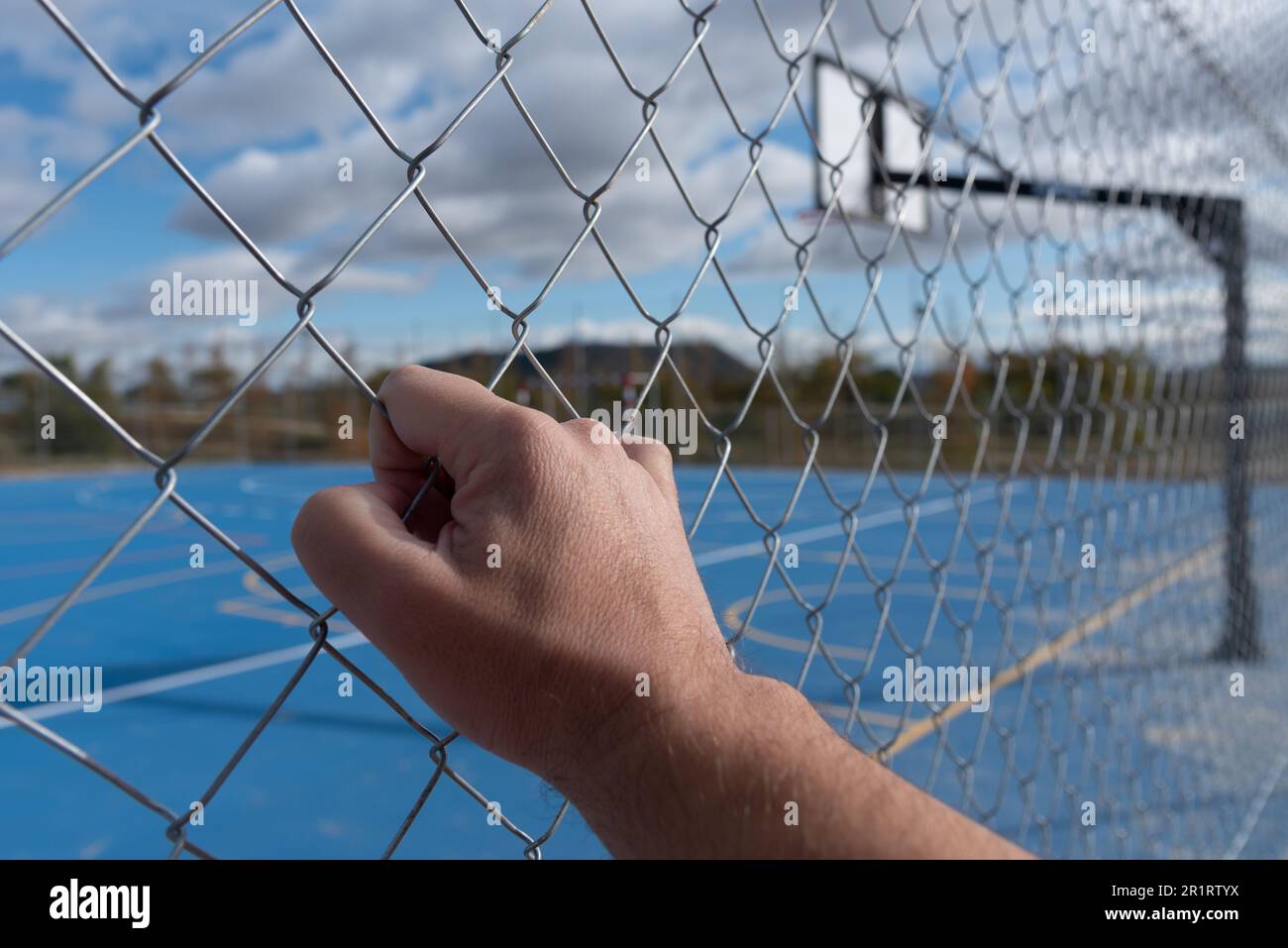 Hand grabbing the outside fence of a blue colored outdoor basketball ...