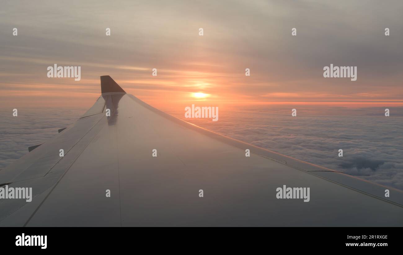 View along jet aircraft wing with orange sun on horizon in flight above clouds Stock Photo - Alamy
