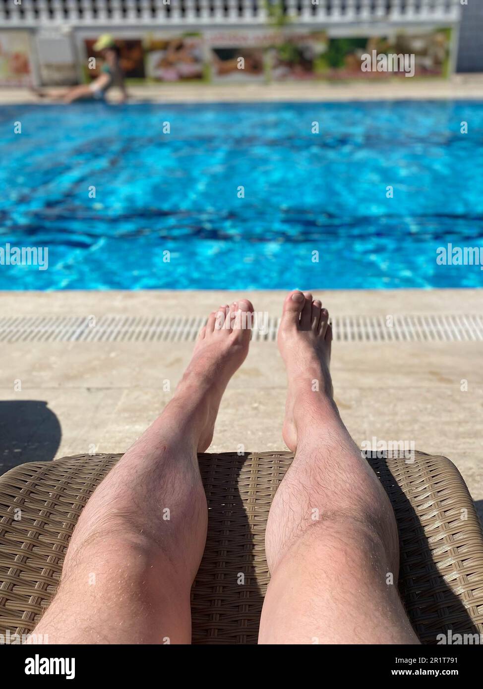 legs of man - male tourist lies on a beach chair during sunset in the swimming pool area of the ...