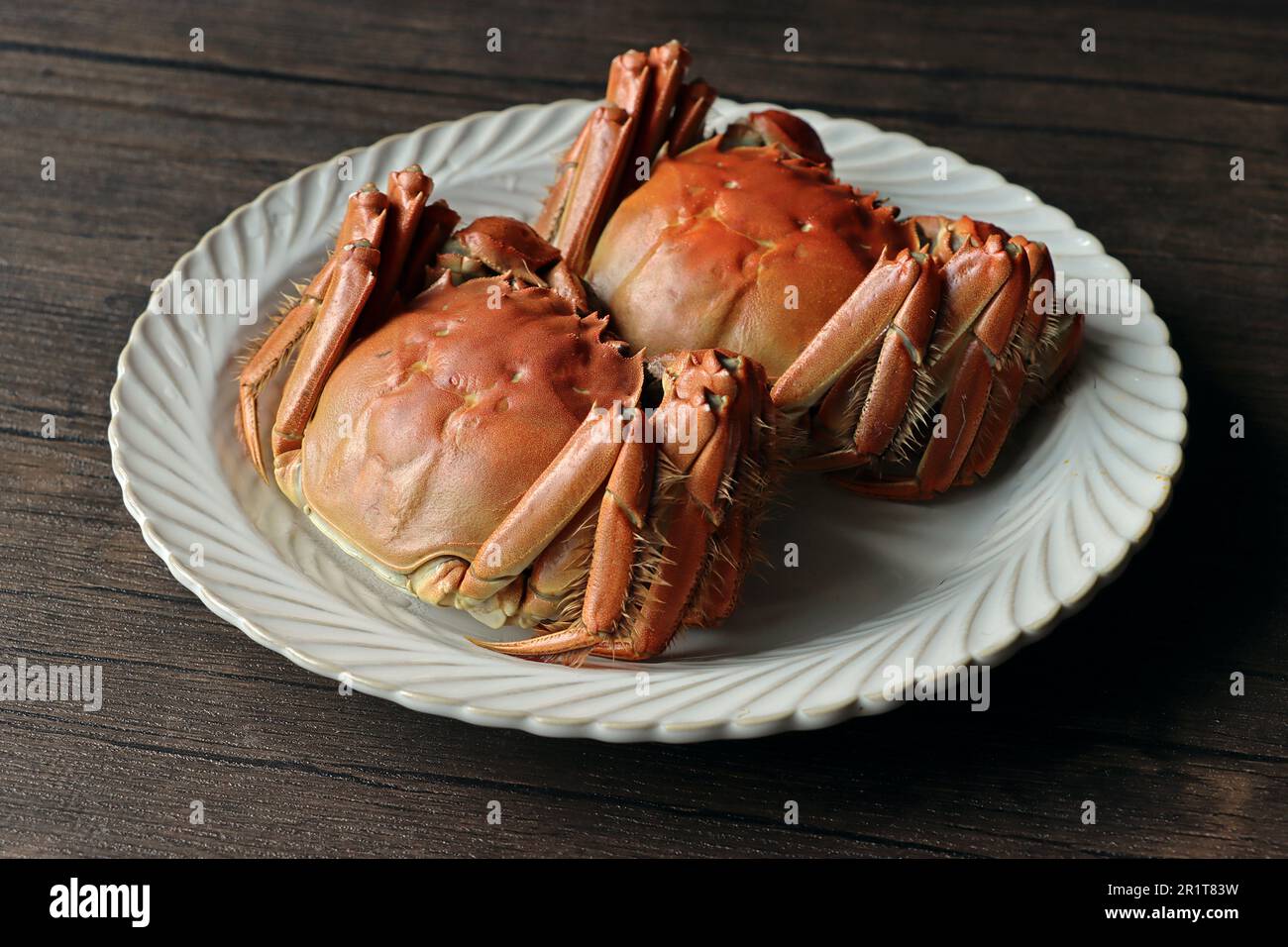 Two large, freshly-cooked hairy crabs on a white plate atop a textured ...