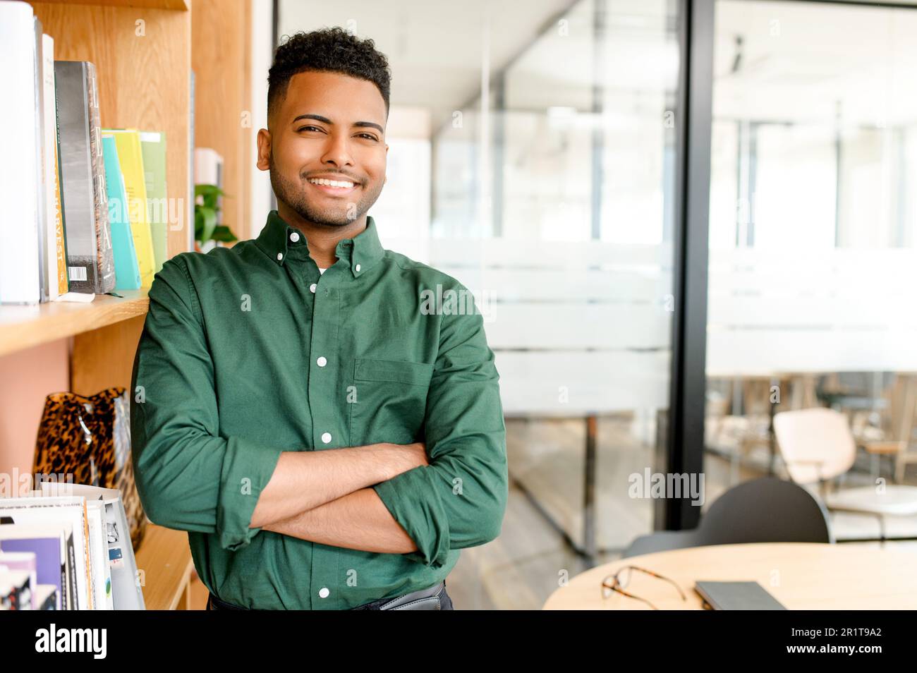 Smiling young indian businessman stands near desk and looks at the ...